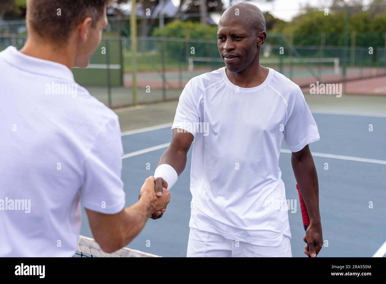 Diverse male tennis players shaking hands on tennis court Stock Photo ...