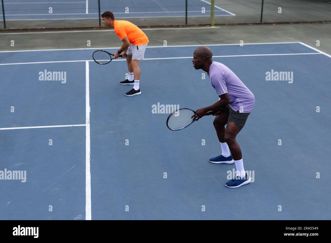 Diverse male tennis players playing doubles on outdoor court Stock ...