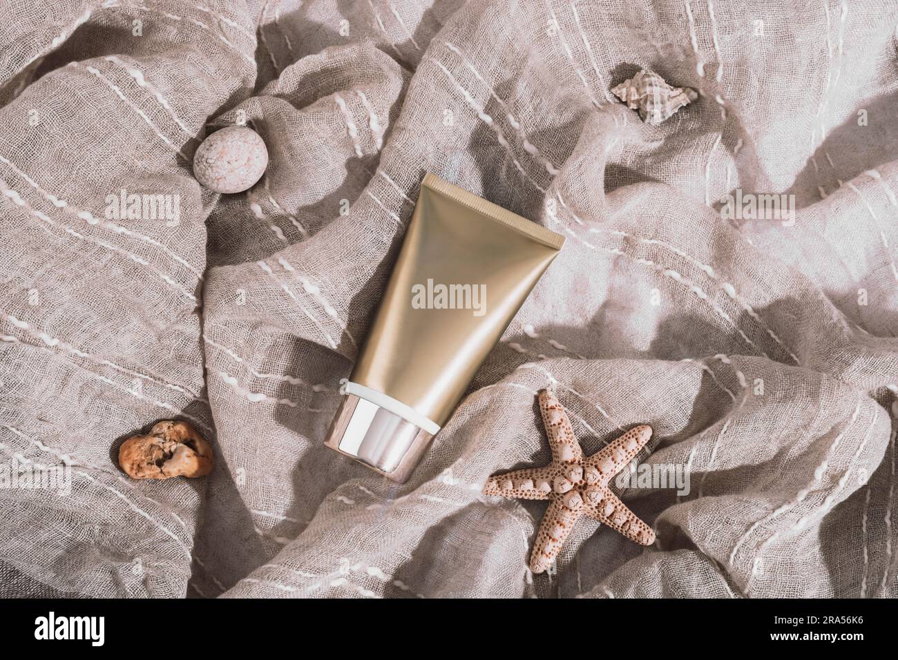 Golden cream tube and seashells on beige cotton fabric in sunlight. Top ...