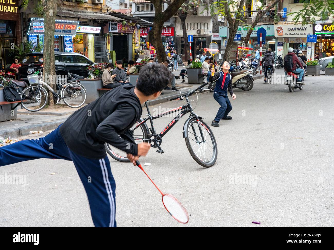 Two boys playing badminton, using a bicycle as a net, in a public ...