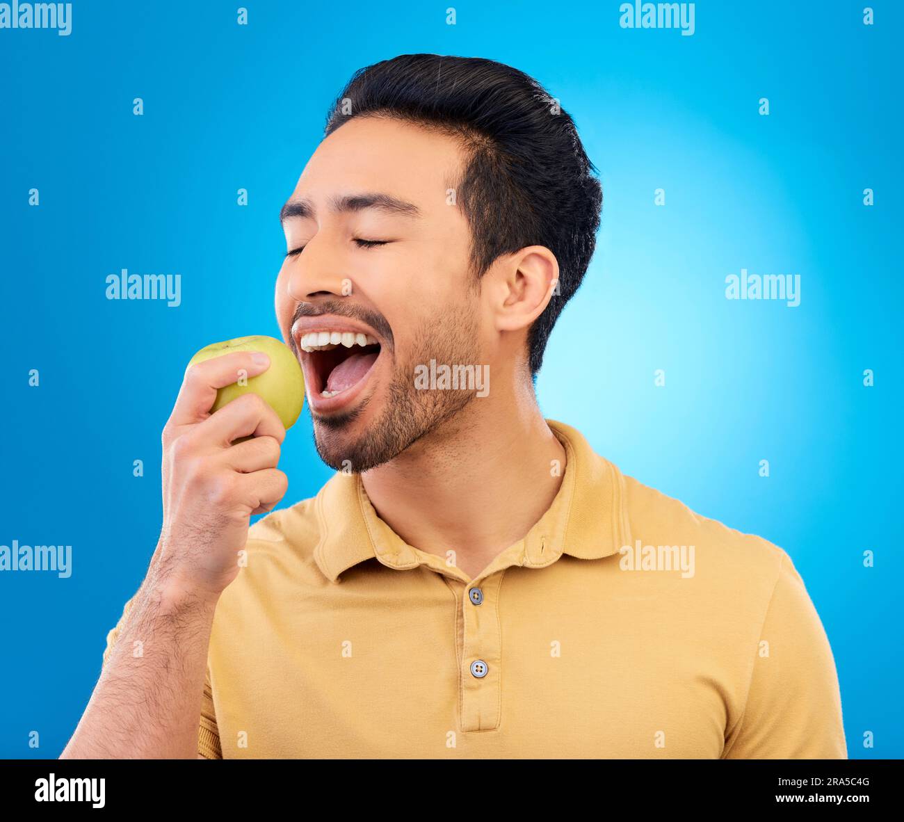 Hand, man eating an apple and against a blue background for healthy ...