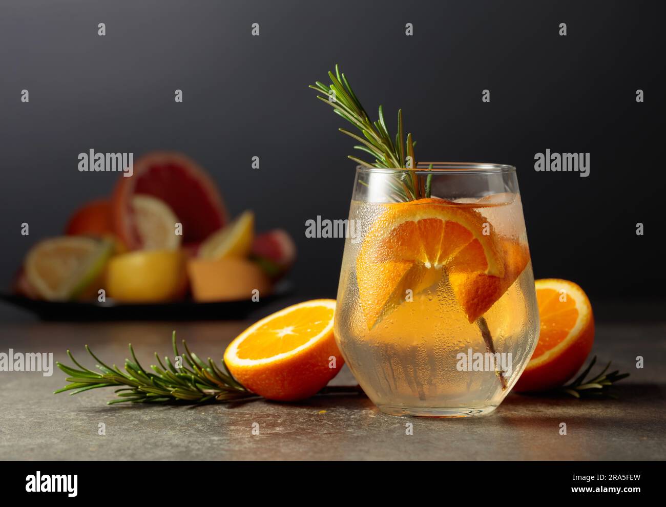 Cocktail gin tonic with ice, rosemary, and orange on a stone table. In ...