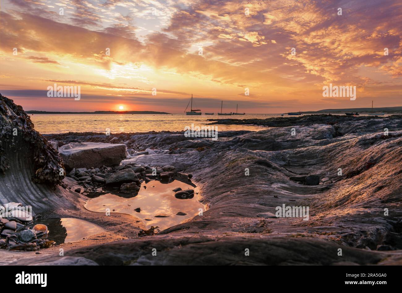 The sun sets over the headland and illuminates the weathered stone and ...