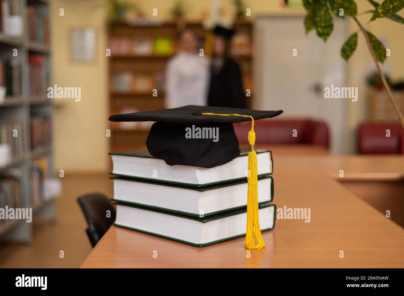Graduation cap on a stack of books in the library Stock Photo - Alamy