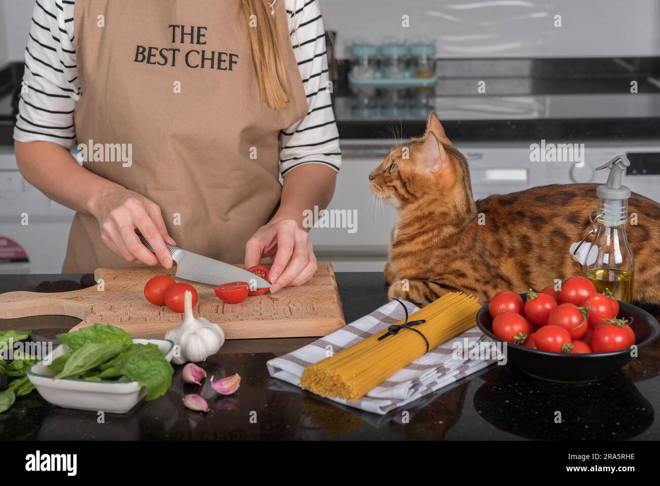 The cat and her owner prepare pasta with cherry tomatoes and basil. The ...
