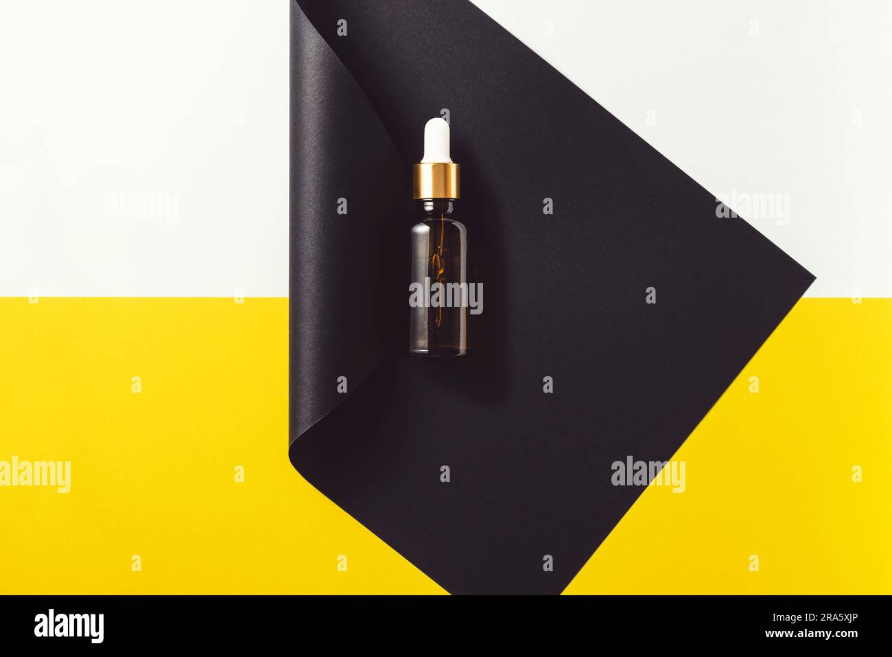 No name glass oil dropper bottle on black folded paper, yellow and ...
