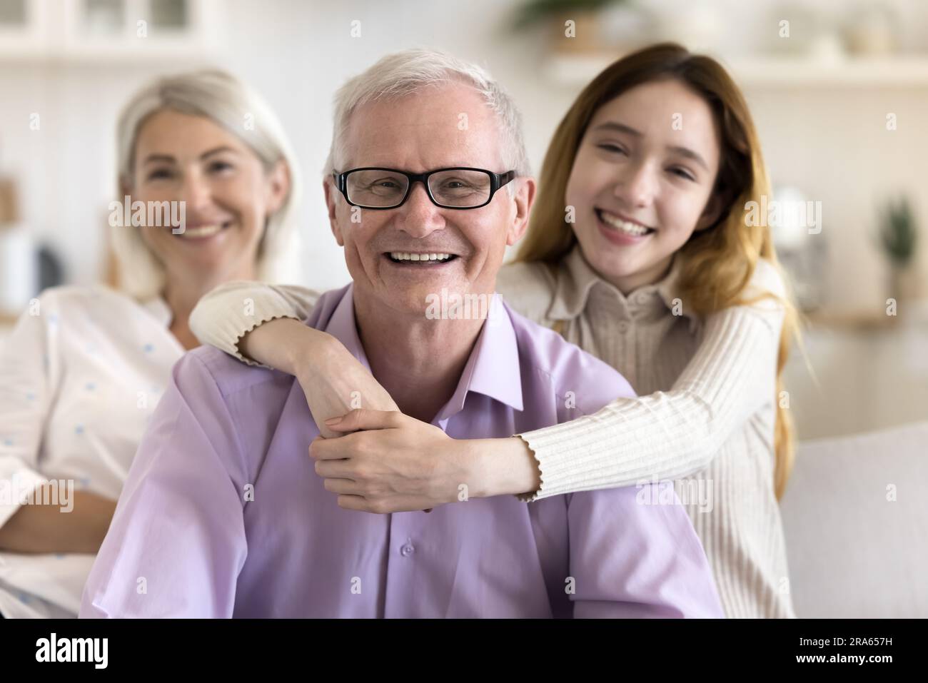 Happy positive grandfather posing at camera with hugging teenage ...