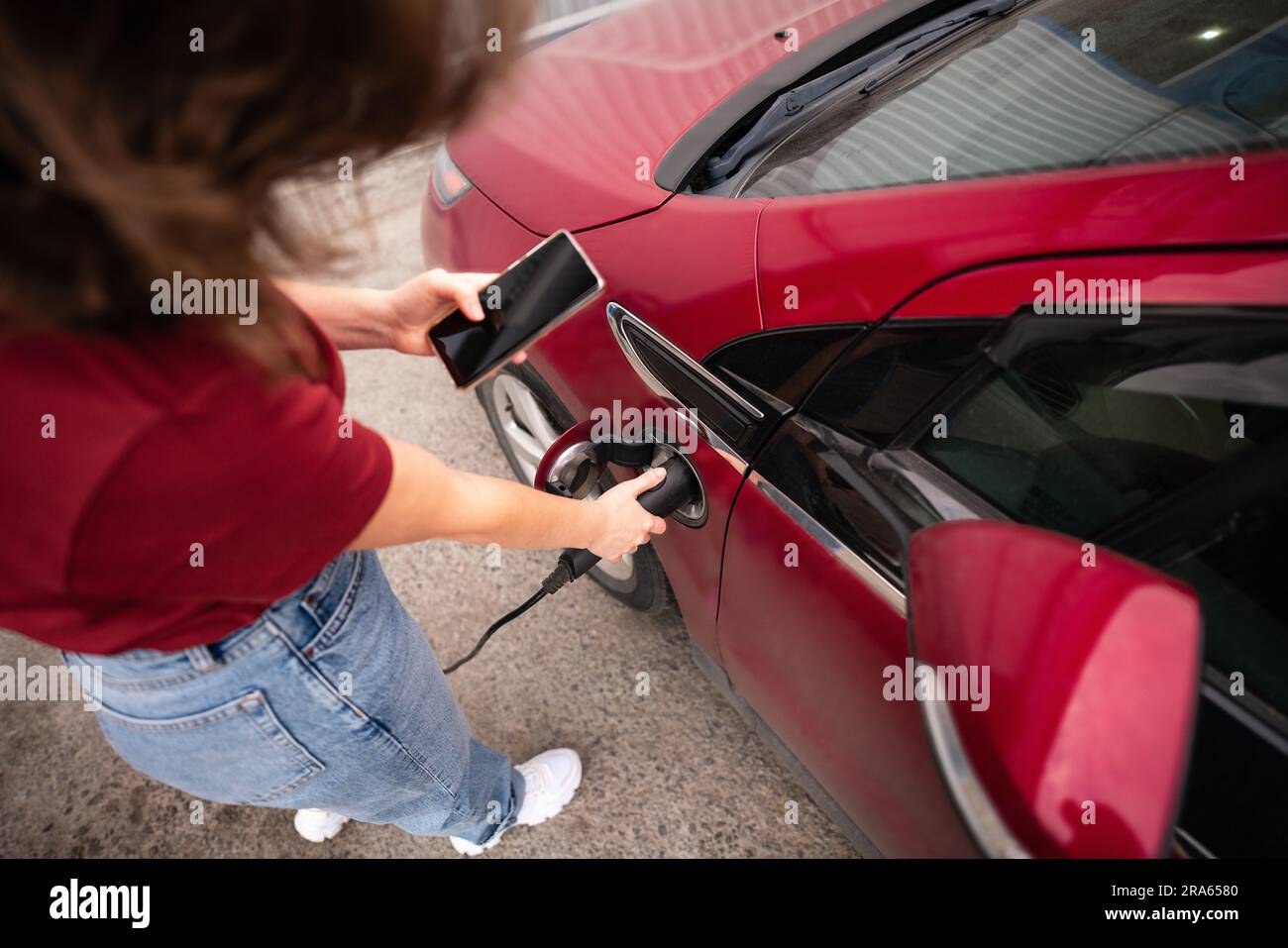 Woman with smartphone charging red electric car Stock Photo - Alamy