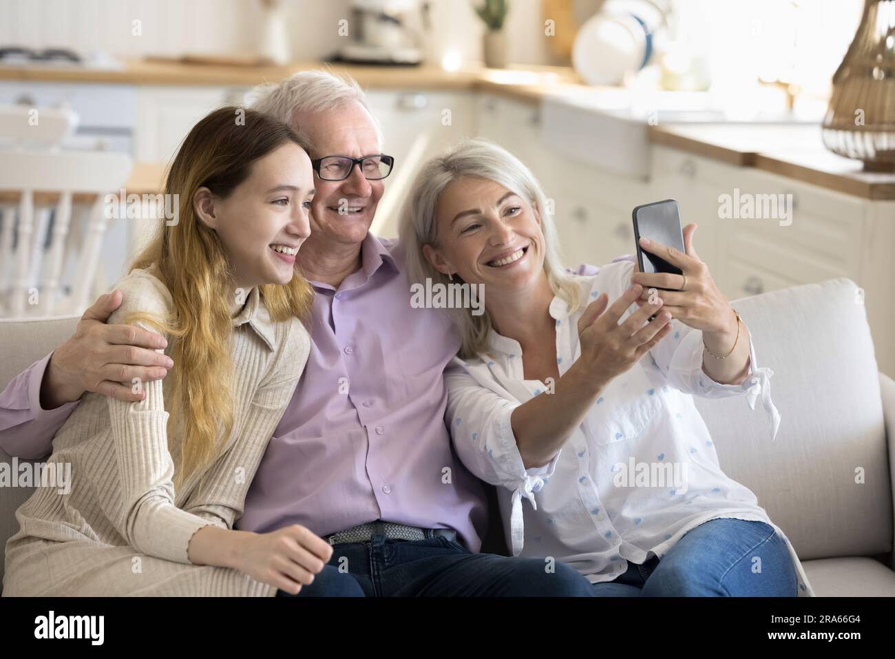 Happy grandma and grandpa hugging teenage child, holding mobile phone ...