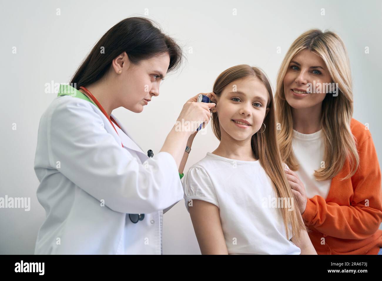 Concentrated woman laryngologist examining ear of little patient with ...