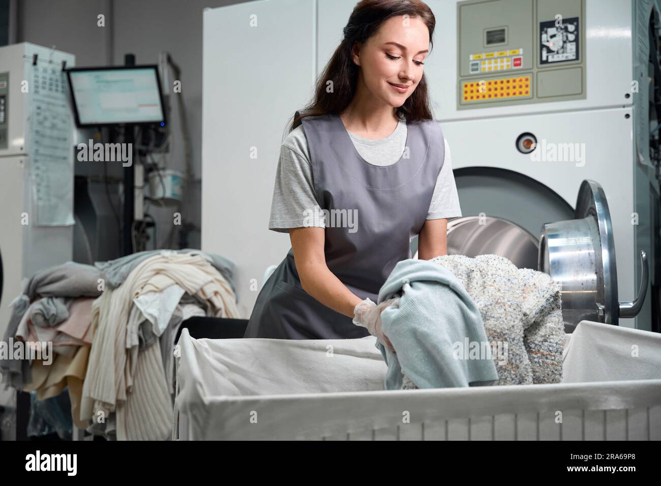 Worker of laundry shop loading industrial washing machine with clothes ...