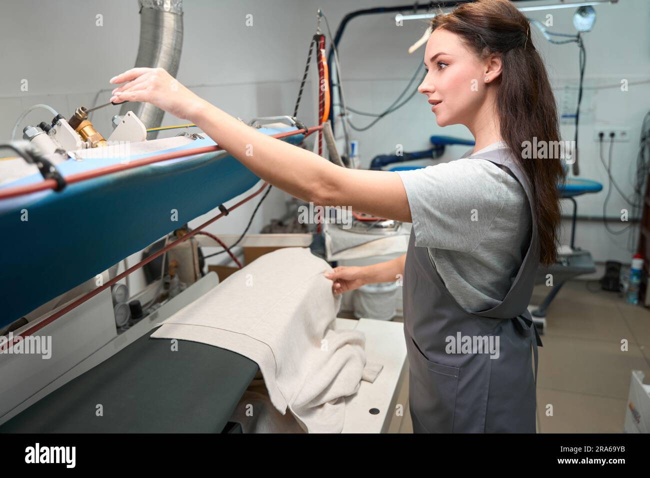 Skilled woman dry-cleaning service worker pressing clothes on special ...