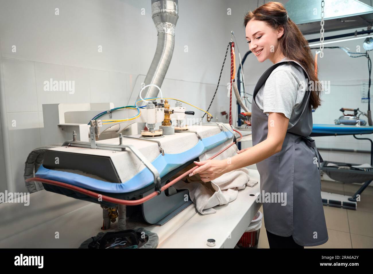 Dry-cleaning office operator ironing clothes with special steam press ...