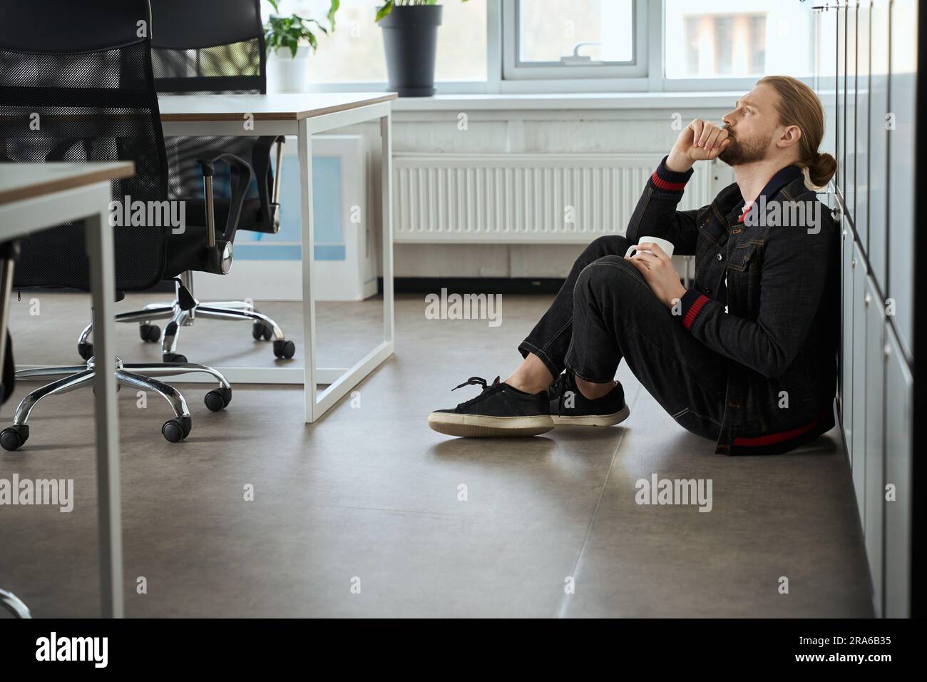 Frustrated employee with cup of coffee sits on the floor Stock Photo ...