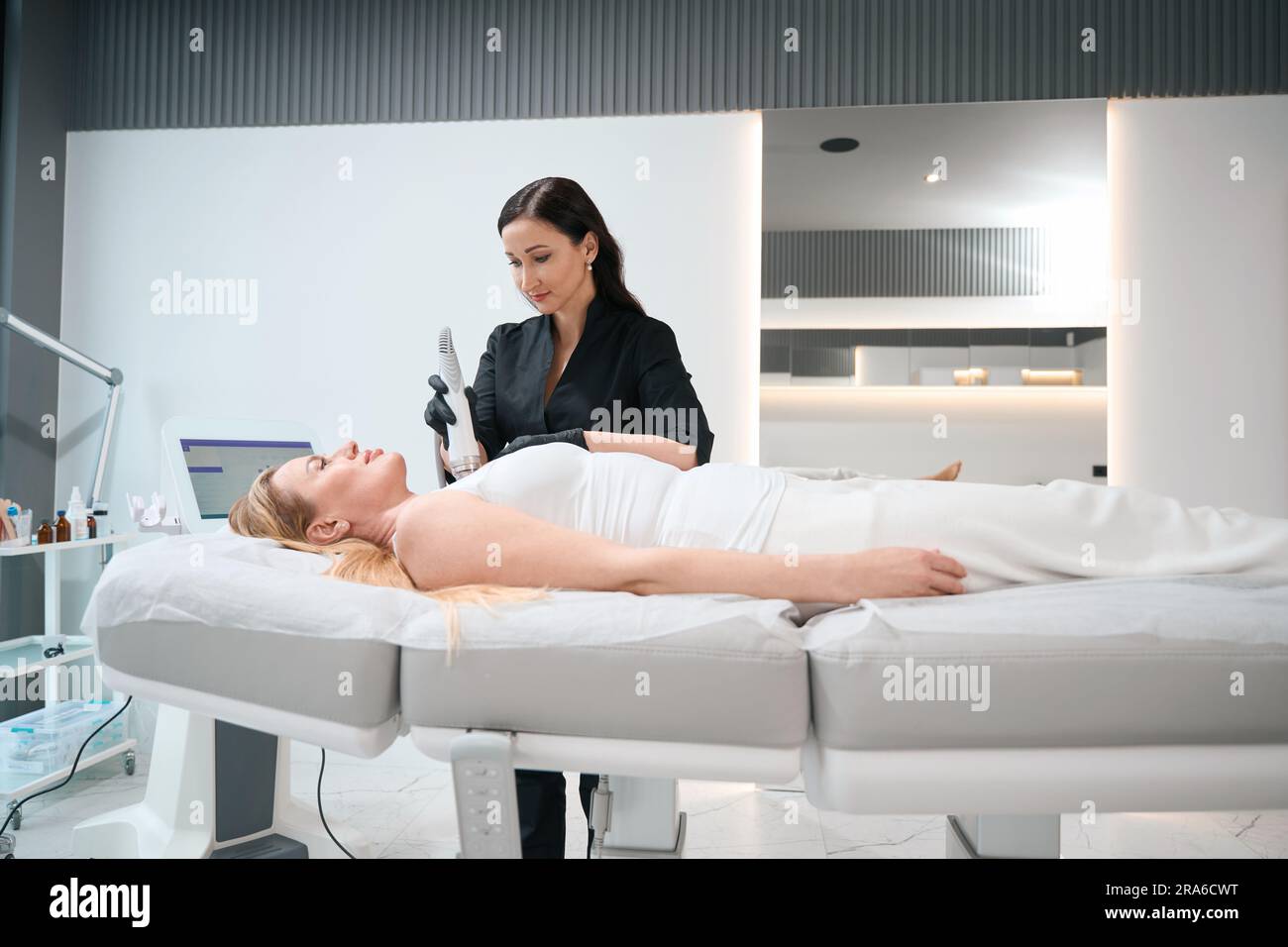 Young cosmetologist performs RF lifting procedure in the decollete area ...