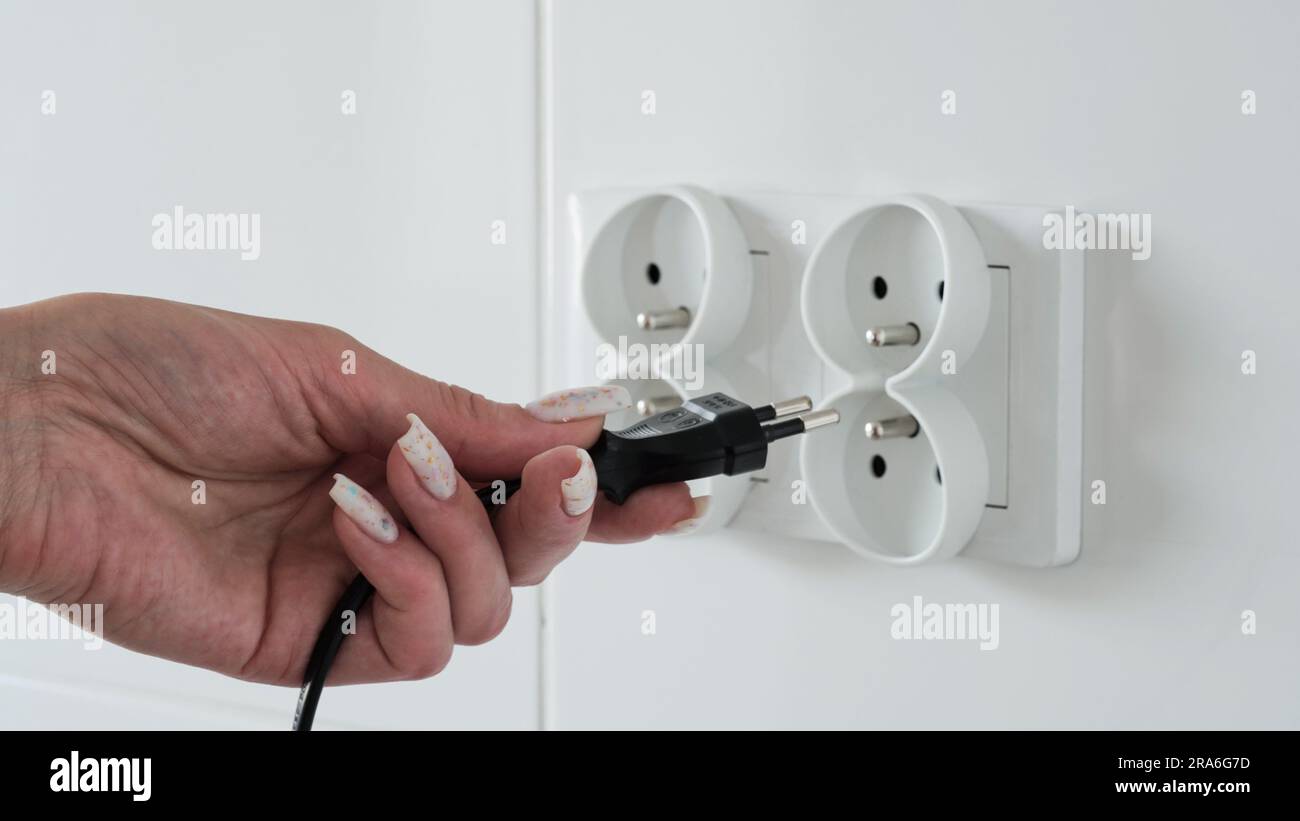 Close-up of a female hand inserting a black electric plug into a double ...