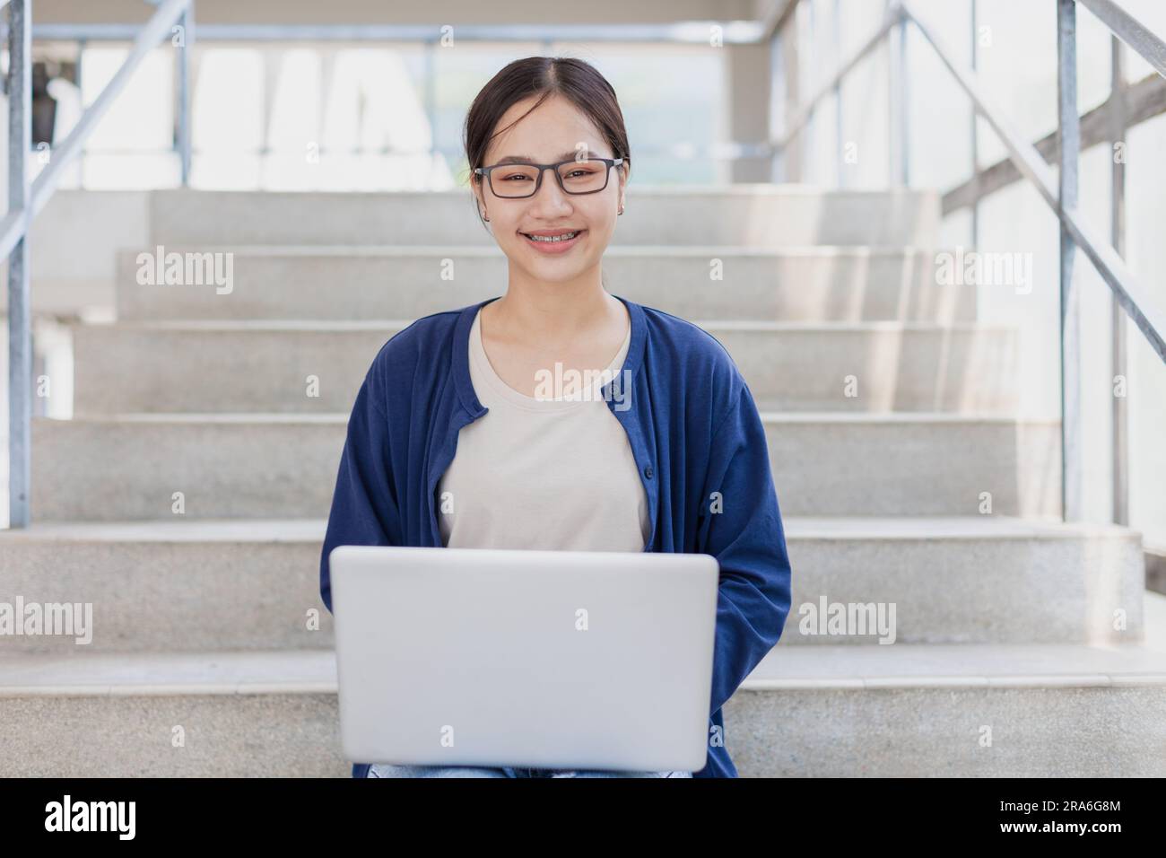 Asian woman sitting at university building stair with laptop computer ...