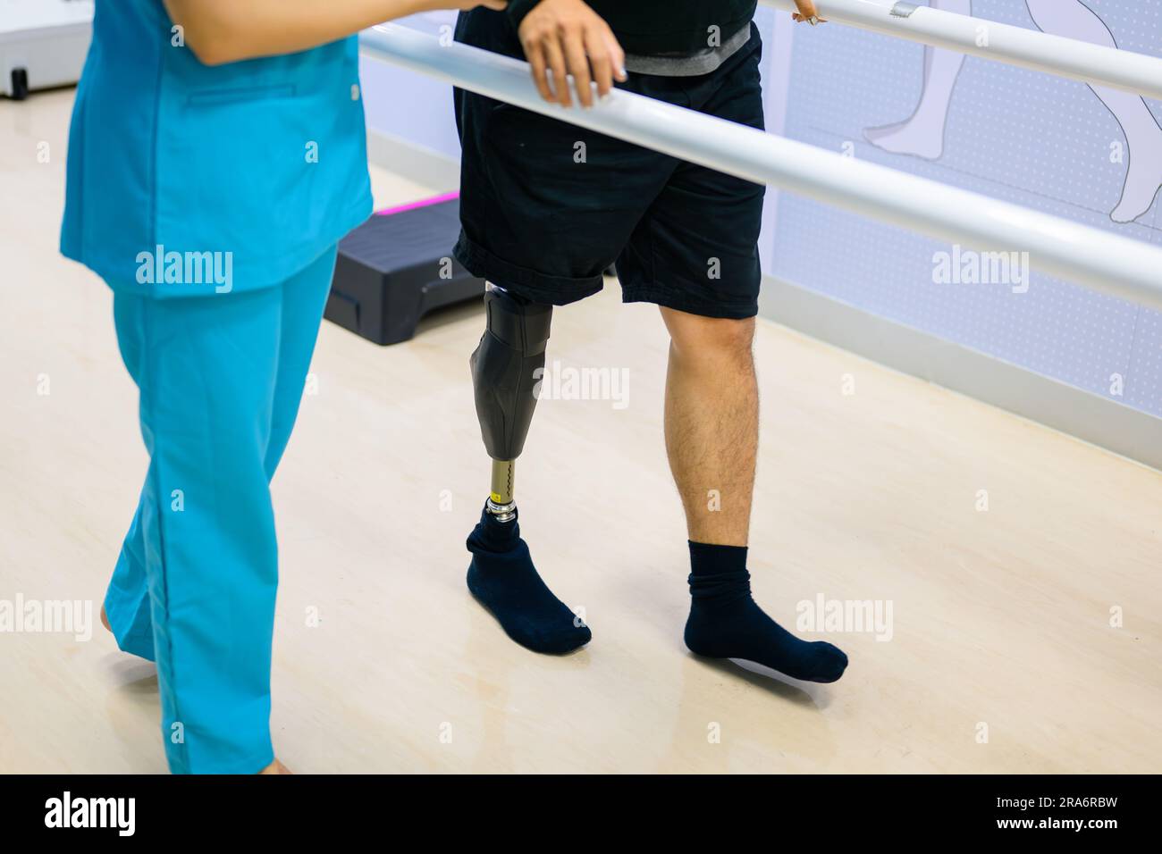 Physiotherapist helping patient with prosthetic leg at parallel bars ...