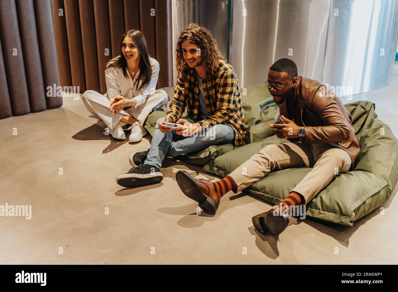 One female and two male multiracial colleagues sitting on lazy bags ...