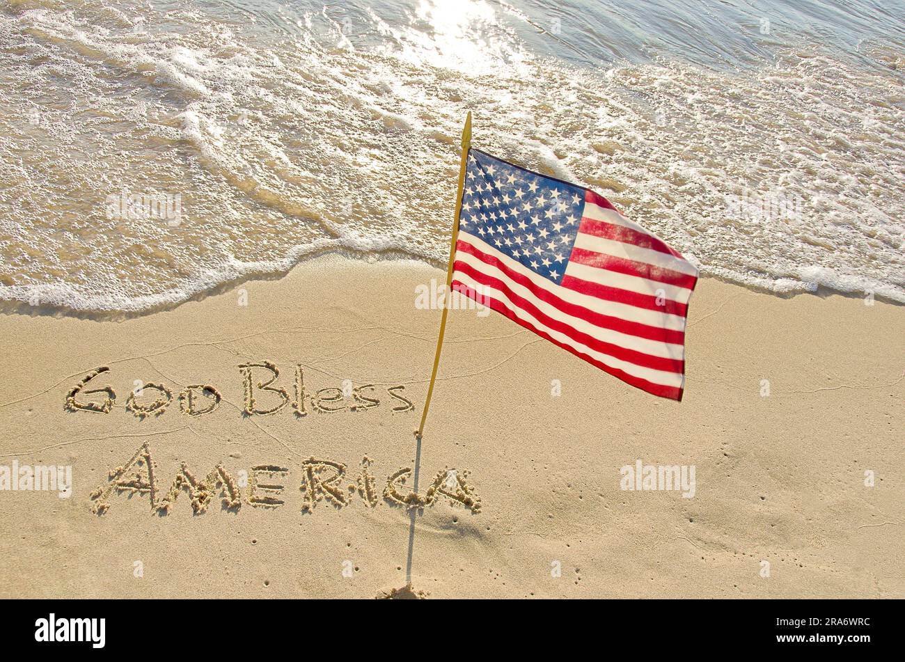 God Bless America text in beach sand with an American flag on sunshine ...