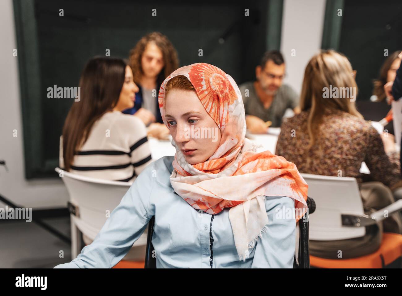 Concentrated disabled female employee wearing hijab working on lap top ...