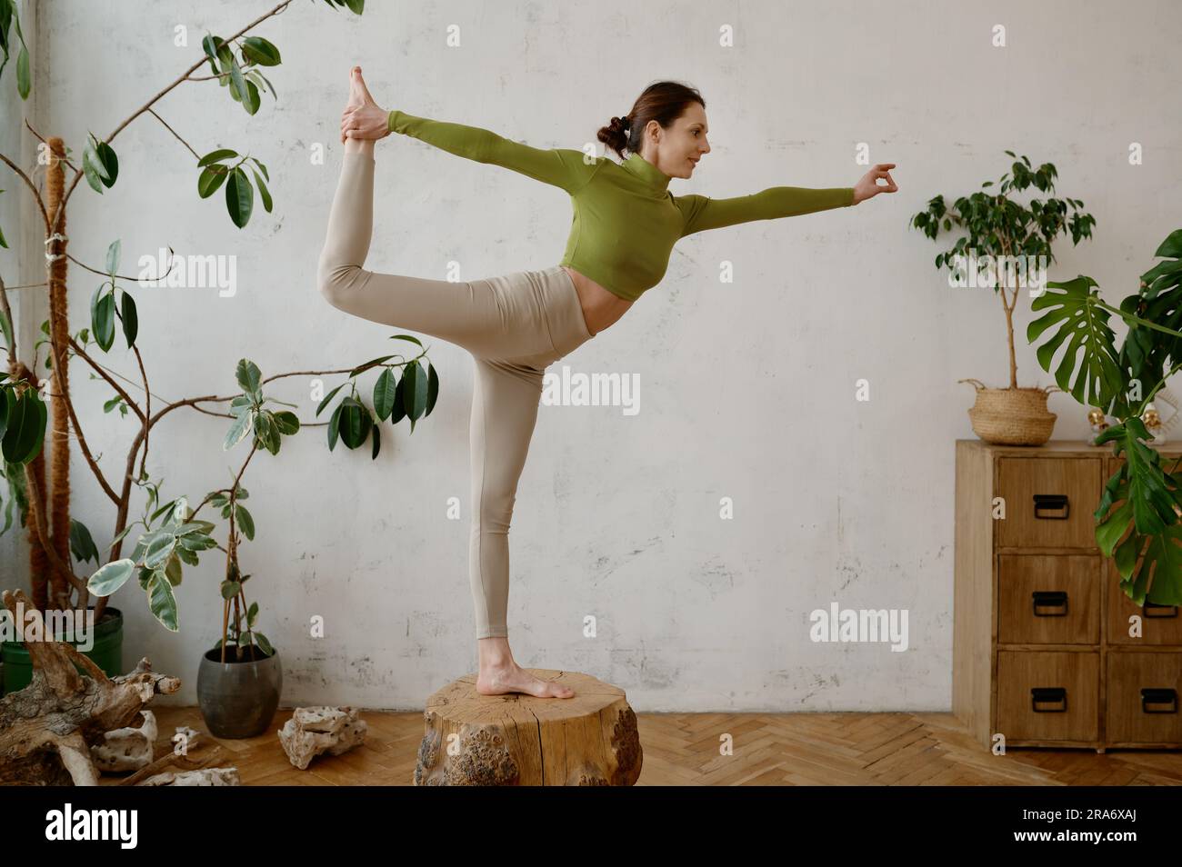 Young strong woman balancing on wooden stump in dancer yoga pose ...