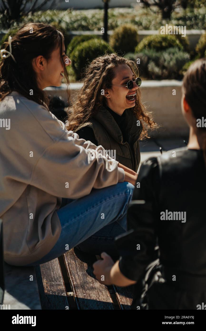 Three cute girls sitting on a bench, having a conversation and laughing ...