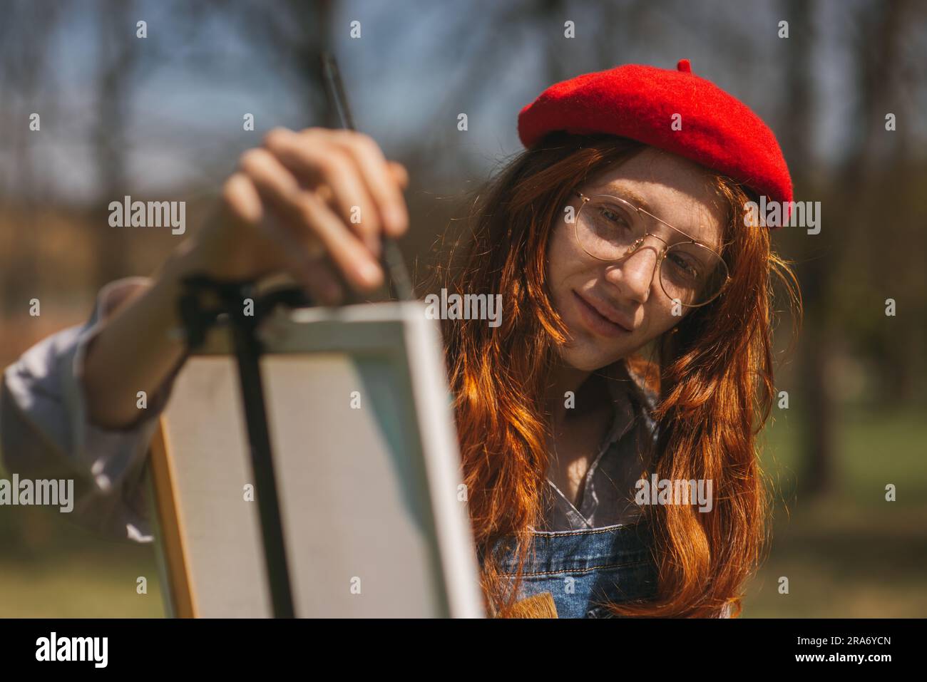 Close up of a beautiful ginger girl with red beret painting on a canvas ...