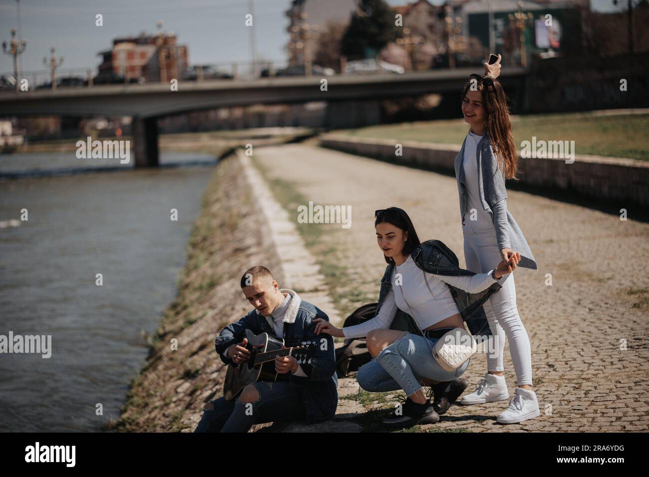 Three friends having fun ,laughing and playing guitar next to the river ...