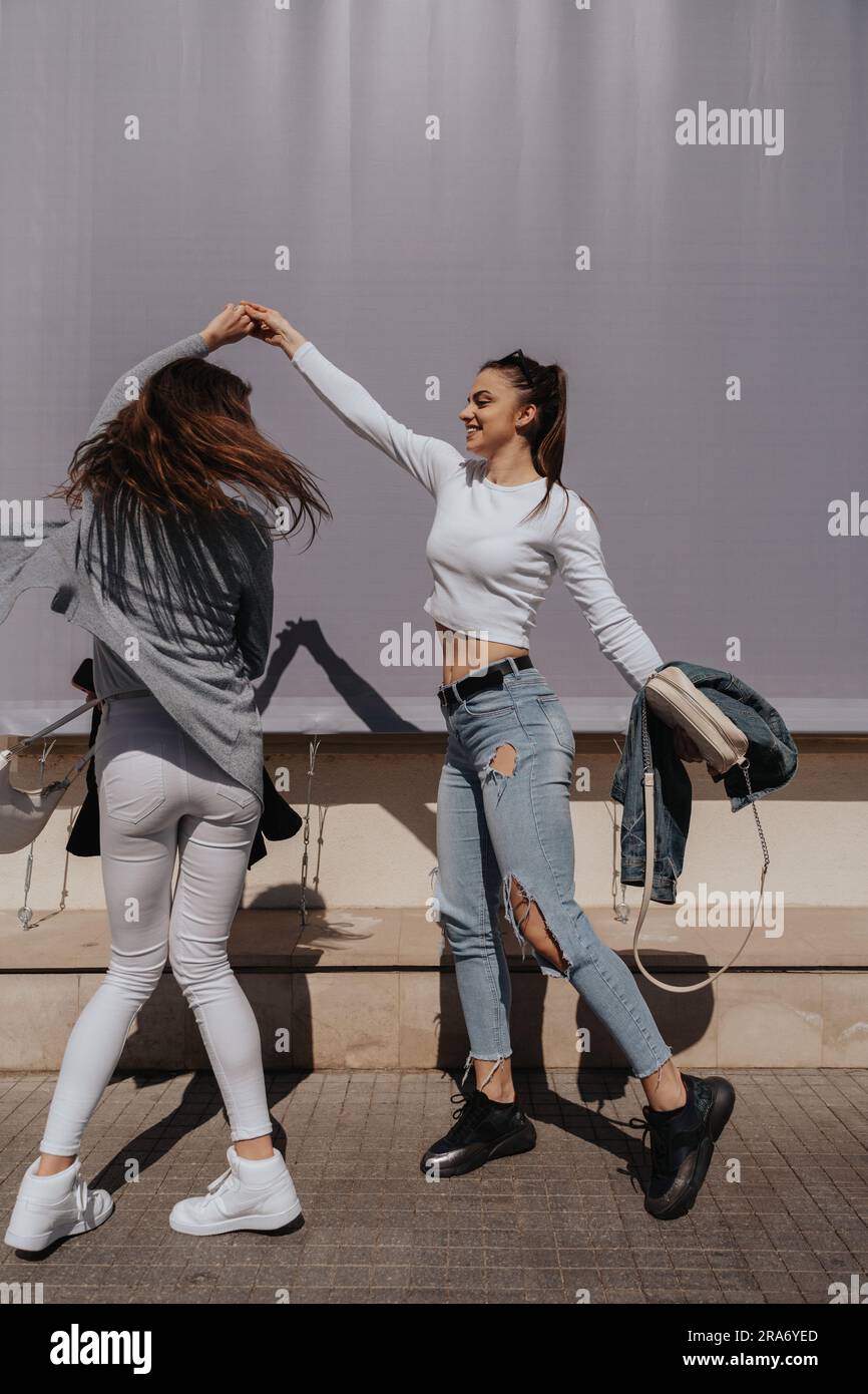 Two pretty brunette girls dancing together in front of the grey wall ...