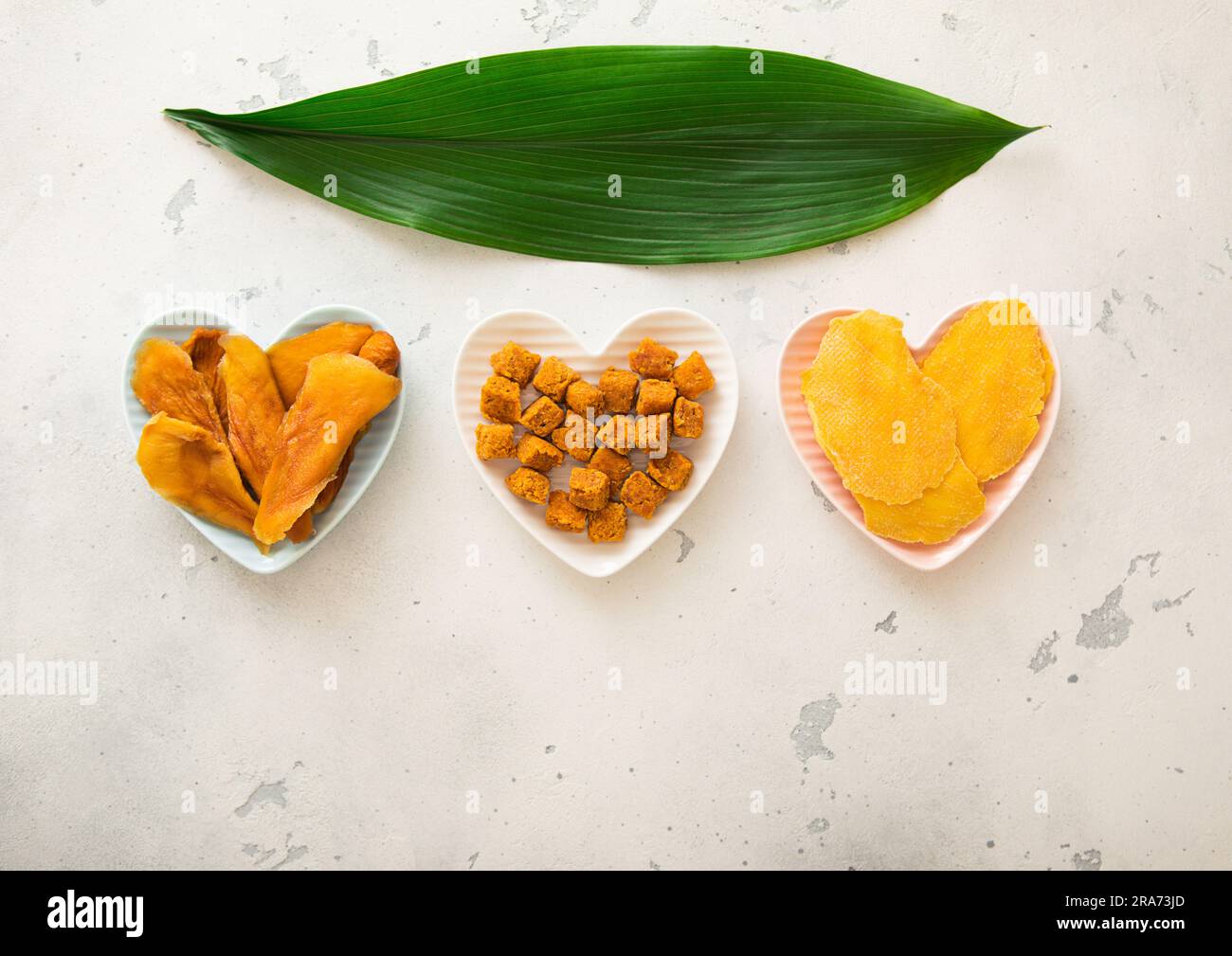Dried mango slices and balls in heart shaped plates on light background ...