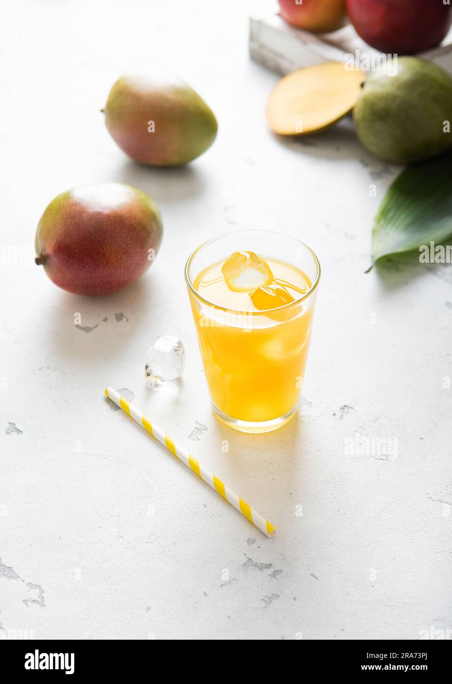 Glass of mango juice with straw and fresh raw organic mangoes on light ...