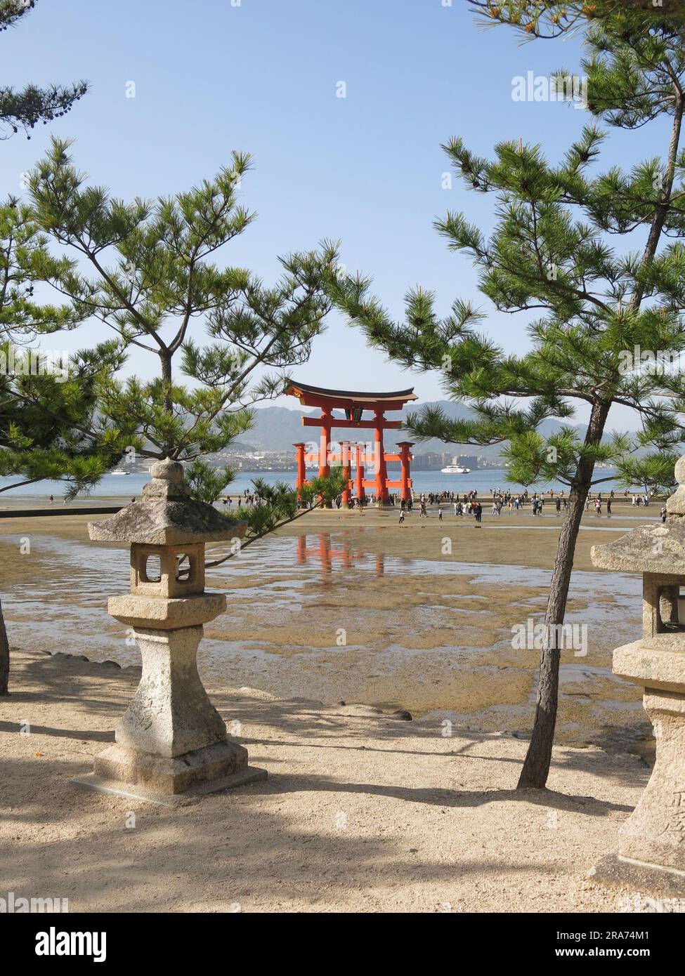 Viewed between two stone lanterns, the red Torii Gate on the beach at ...