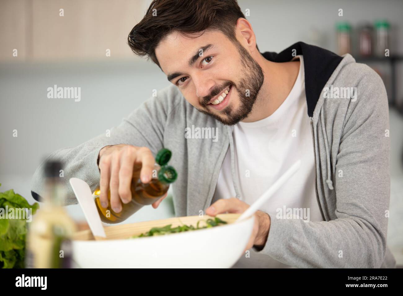 young man adding spice to the salad and smiling Stock Photo - Alamy