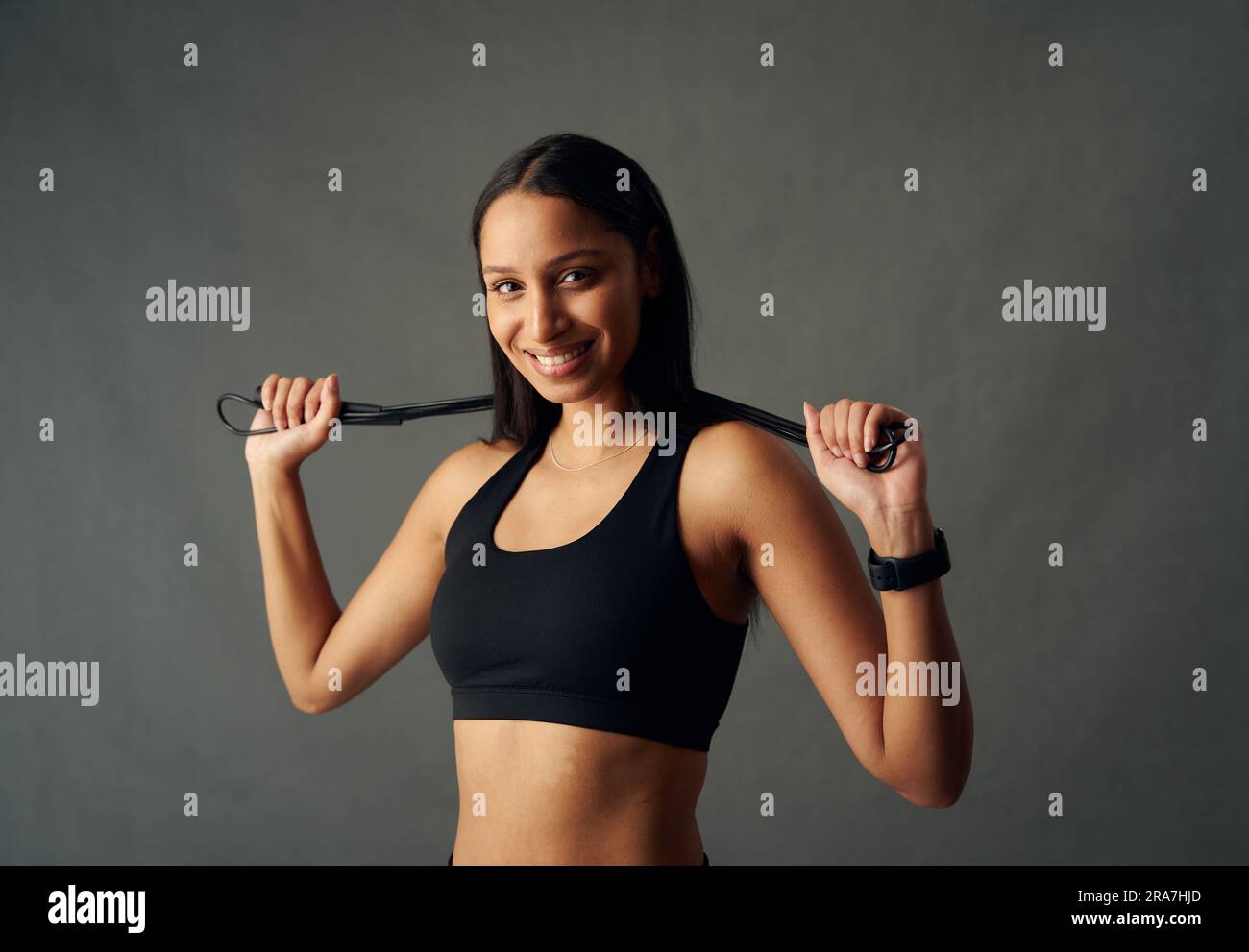 Portrait of happy young biracial woman in sports bra holding jump rope ...