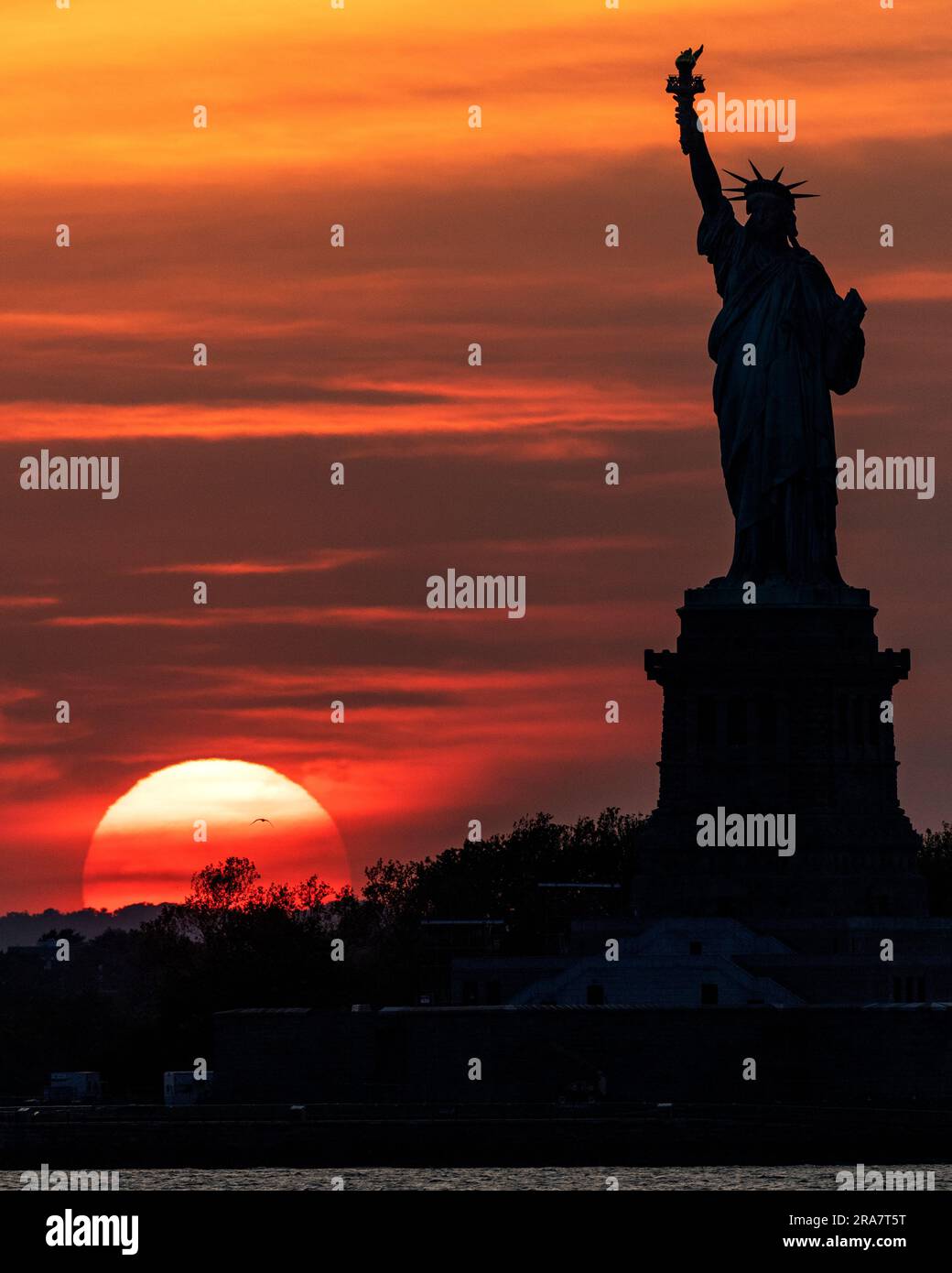 Silhouette of Statue of Liberty with huge setting sun in background and ...