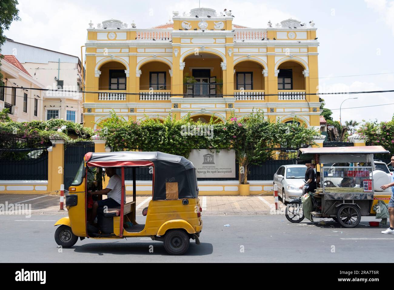 A yellow tuk-tuk passes the UNESCO building in Phnom Penh. Once known ...