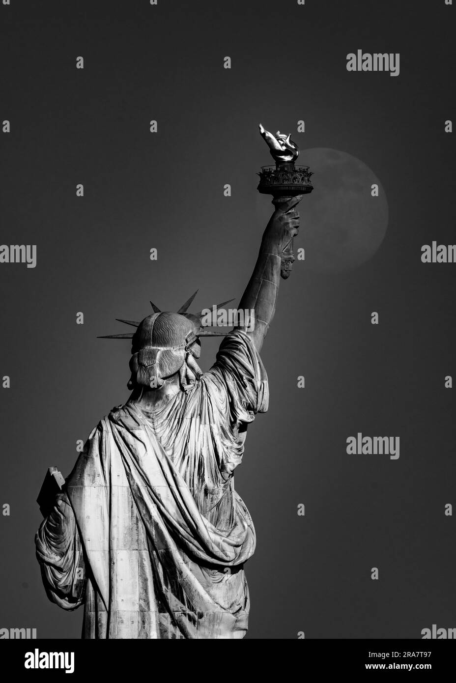 Back of Statue of Liberty with pale moon rising past torch with sharp ...