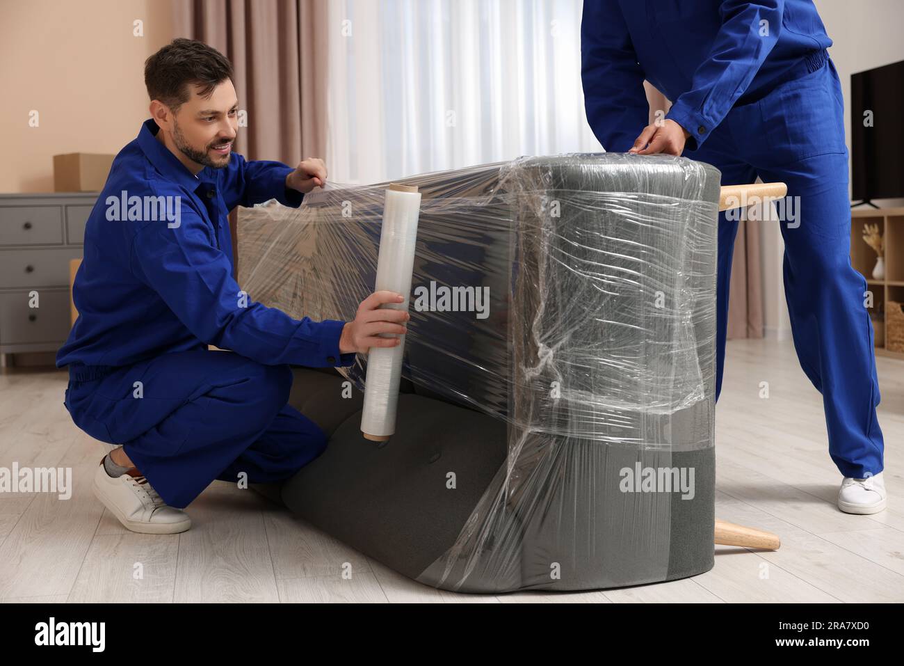 Male movers with stretch film wrapping sofa in new house Stock Photo ...