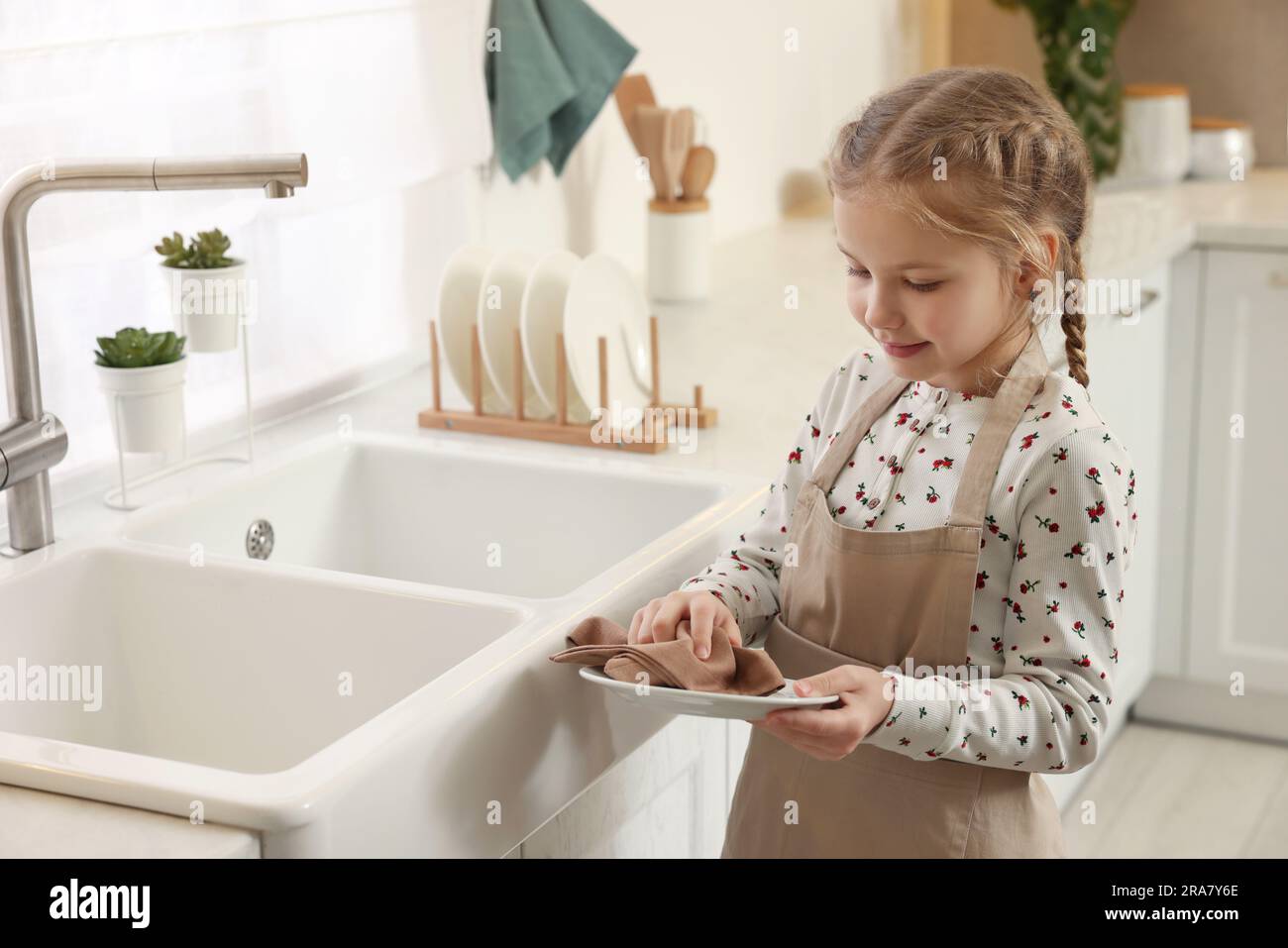 Little girl wiping plate with towel in kitchen Stock Photo - Alamy