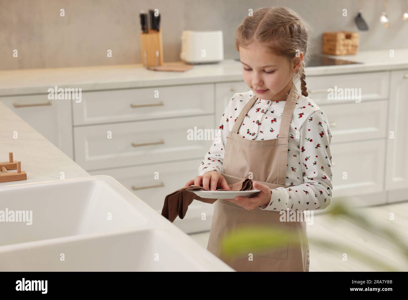 Little girl wiping plate with towel in kitchen Stock Photo - Alamy