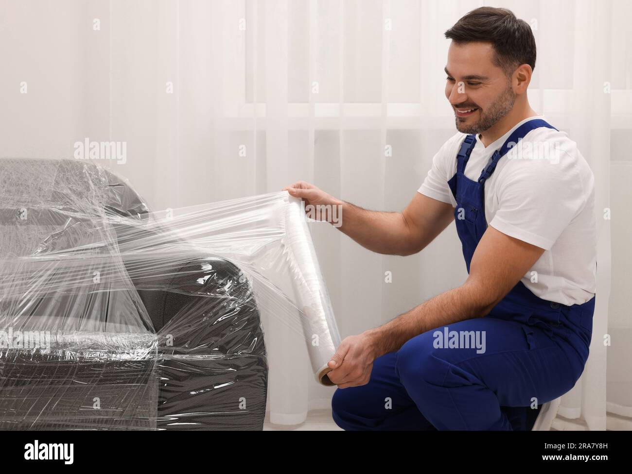 Worker wrapping sofa in stretch film indoors Stock Photo - Alamy