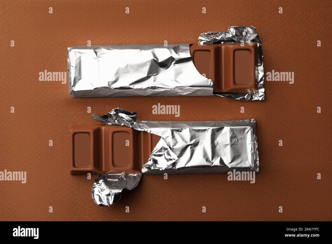 Delicious chocolate bars wrapped in foil on brown background, flat lay ...