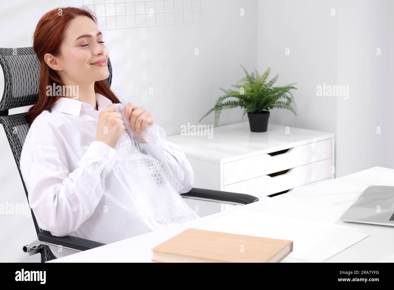 Woman popping bubble wrap at desk in office. Stress relief Stock Photo ...