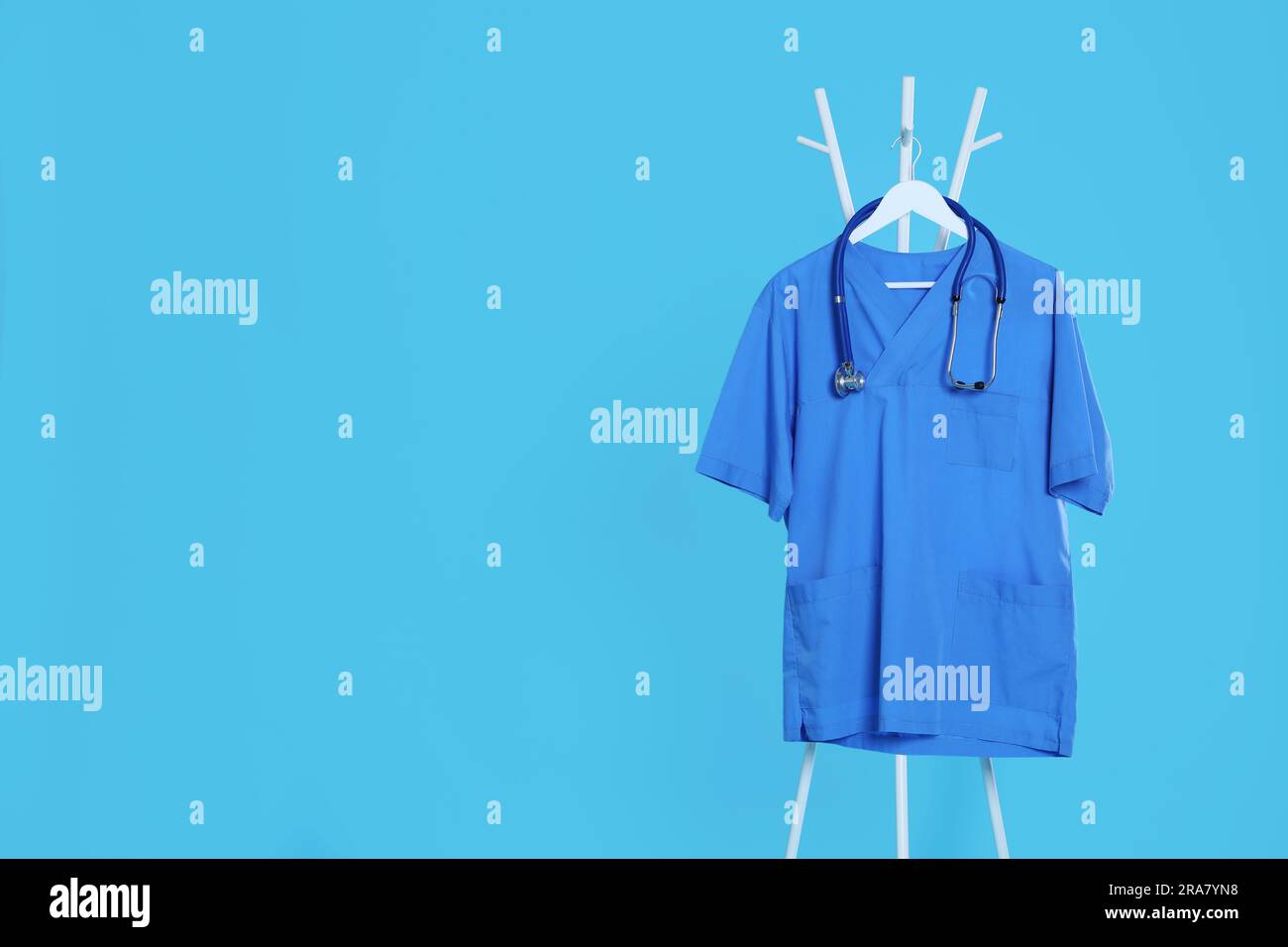 Medical uniform and stethoscope hanging on rack against light blue ...