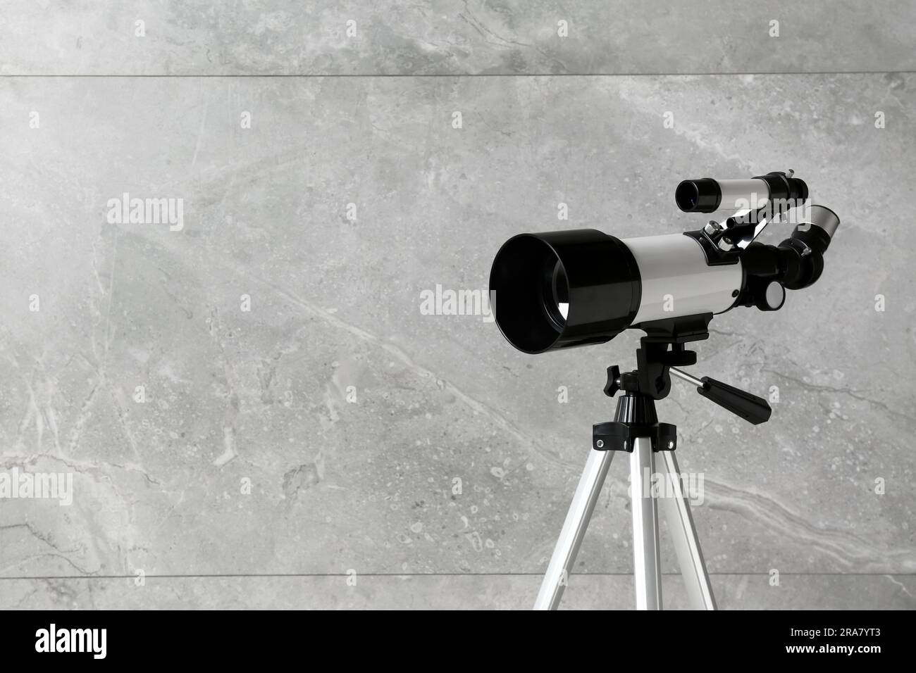 Tripod with modern telescope near grey wall, closeup. Space for text ...