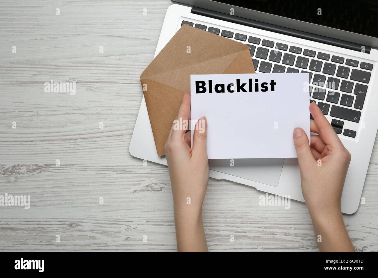 Woman holding letter with word Blacklist near laptop at white wooden ...