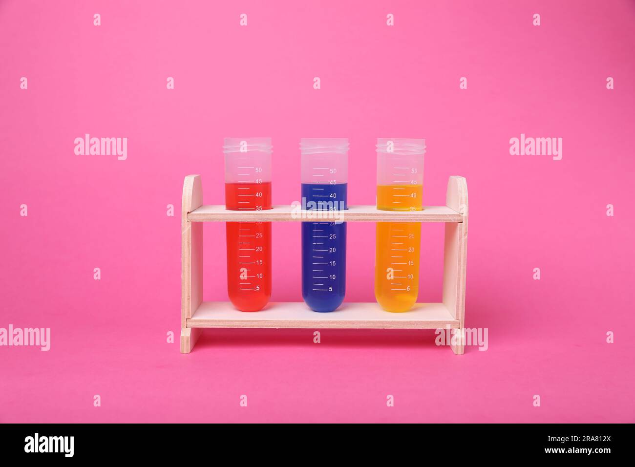 Test tubes with colorful liquids in wooden stand on bright pink ...