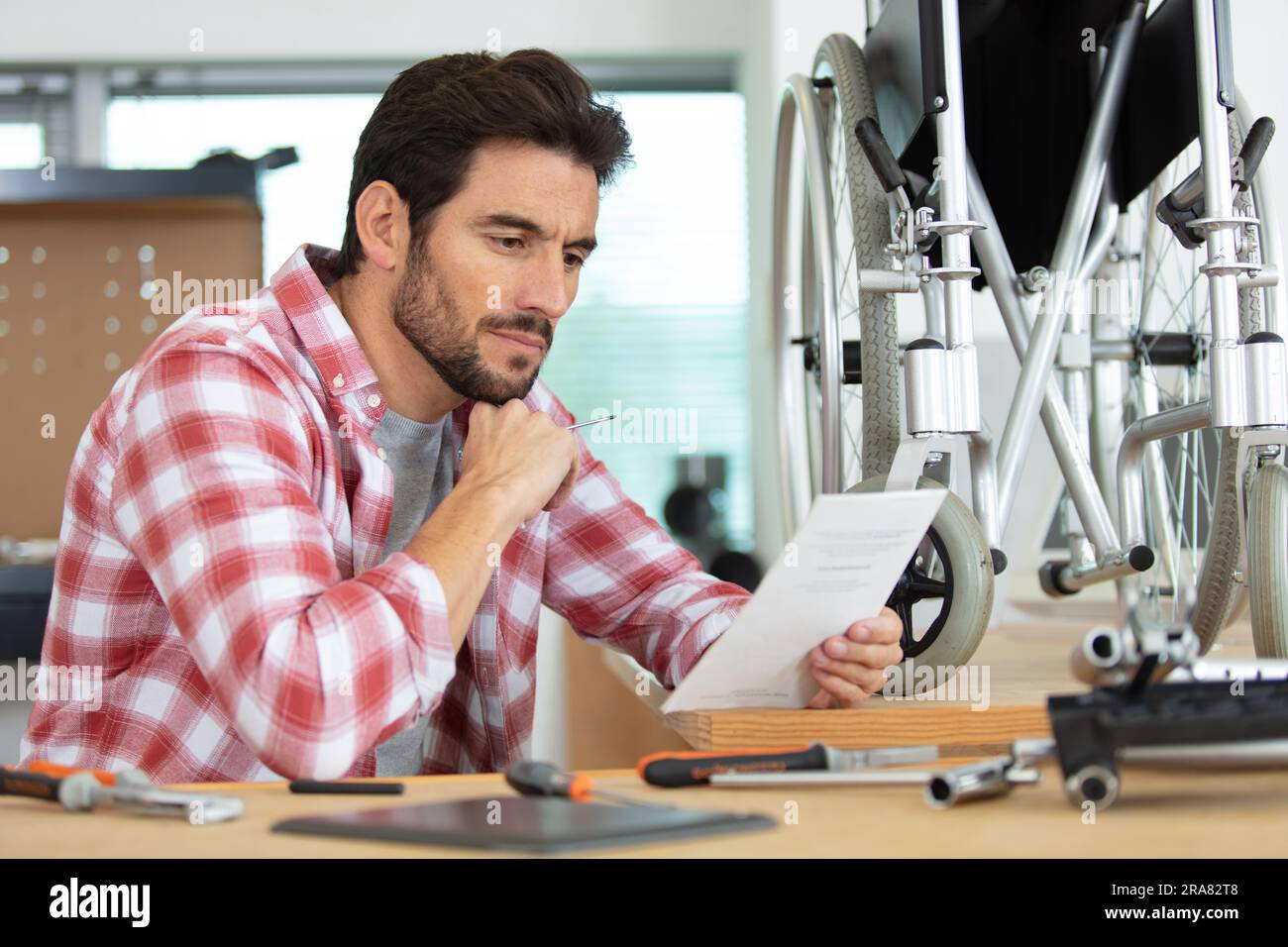 man reading instructions for assembling a wheelchair in a workshop ...