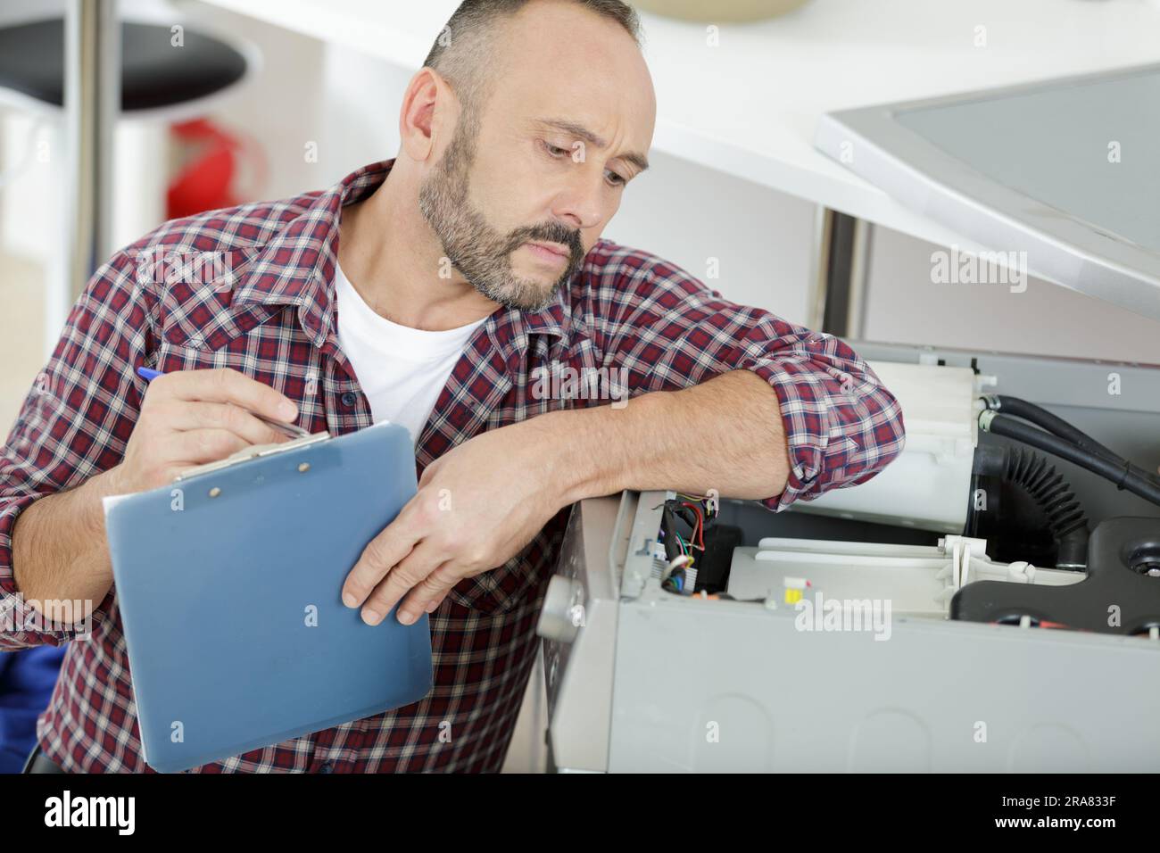 serviceman by washing machine making notes on clipboard Stock Photo - Alamy